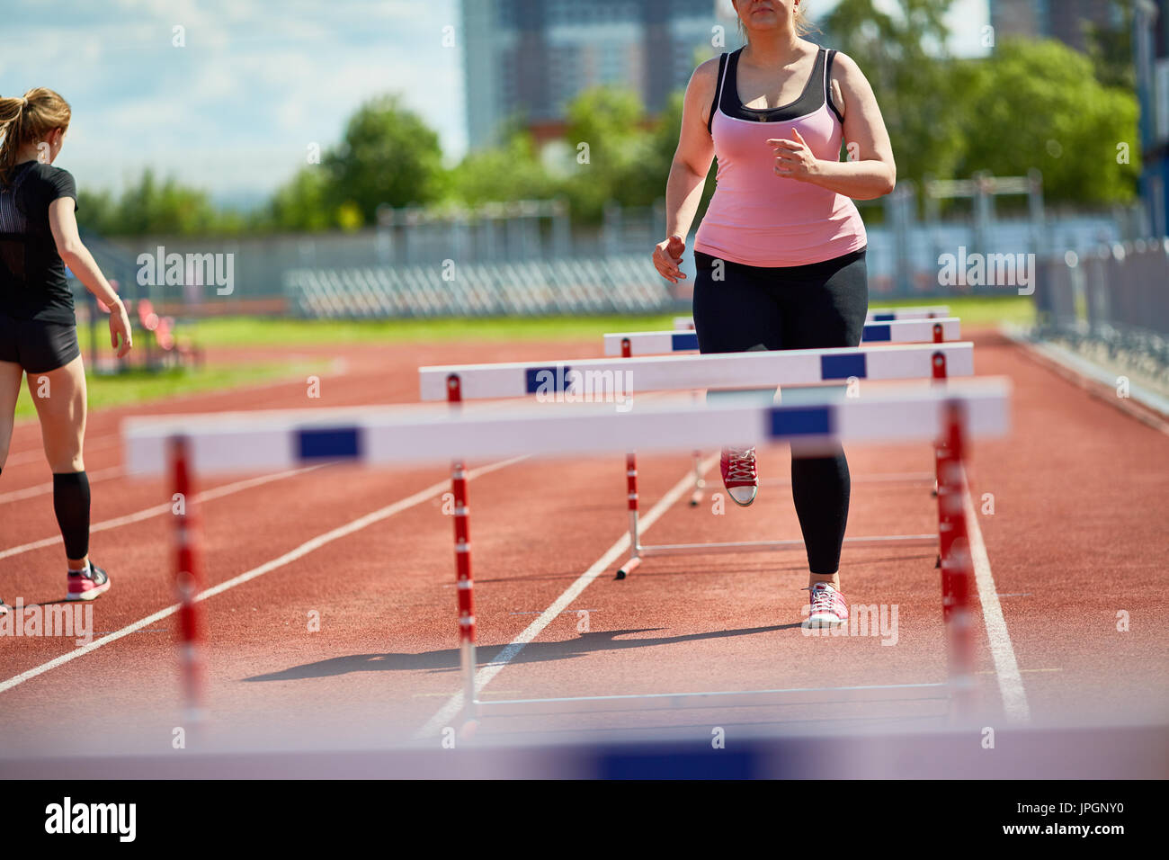 Active obese woman running on racetrack and overcoming hurdles on her ...