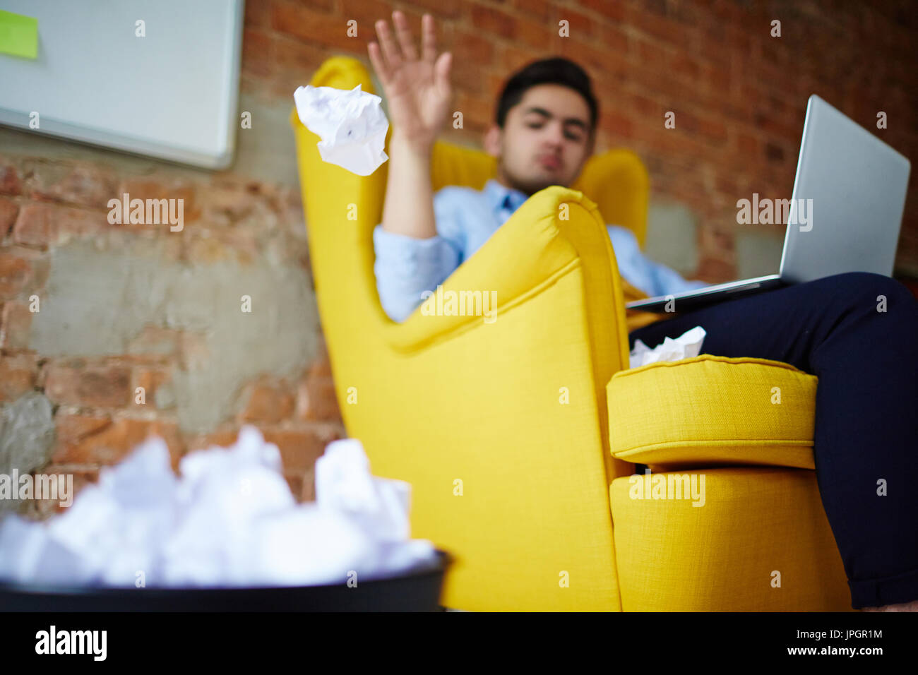 Young man with laptop throwing paper-ball into trash bin Stock Photo ...