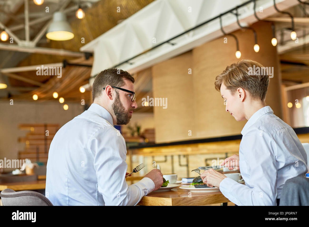 Young colleagues sitting in cafe, having lunch and discussing plans ...