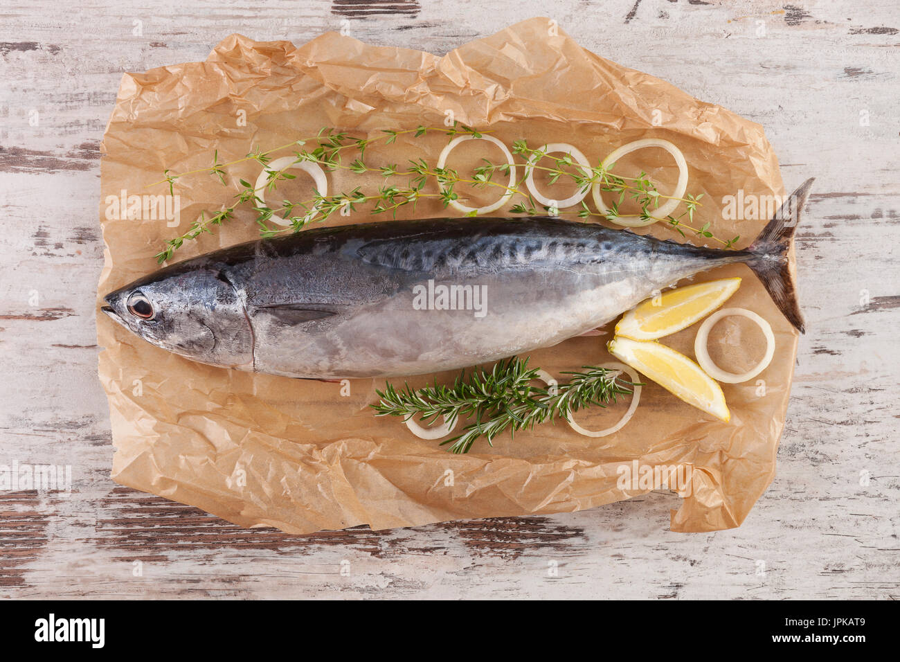 Fresh raw tuna fish on baking paper with onion, herbs and lemon ...