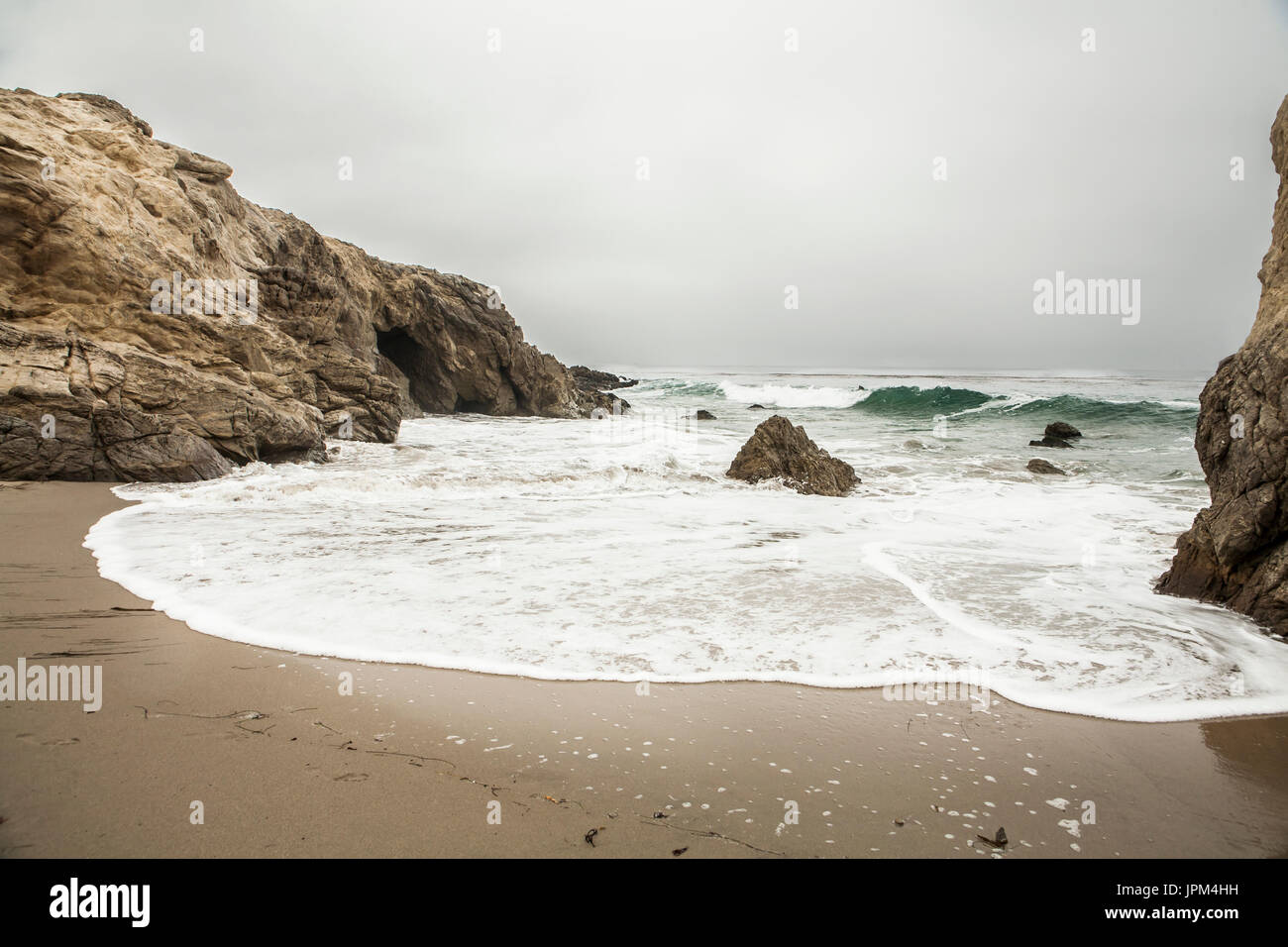 ocean at shore between rocks with rock in middle and a wave coming in ...