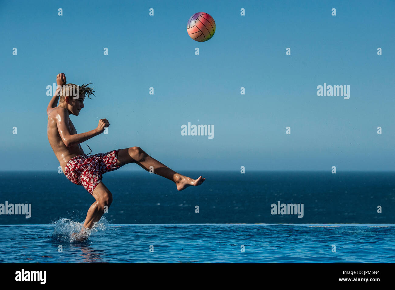A boy jumps to kick a ball in an infinity pool in the summer, playing ...