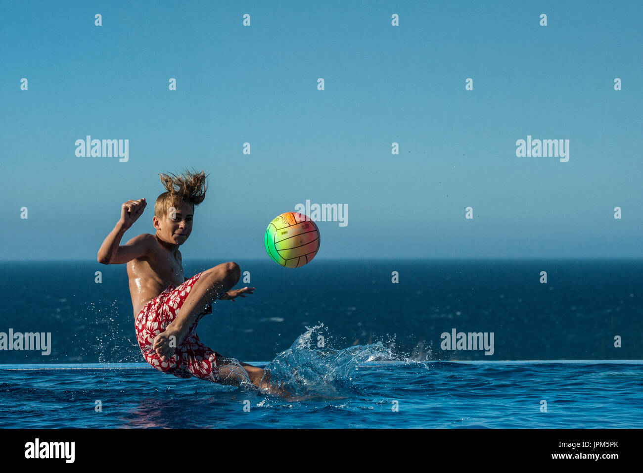 A boy jumps to kick a ball in an infinity pool in the summer, playing ...