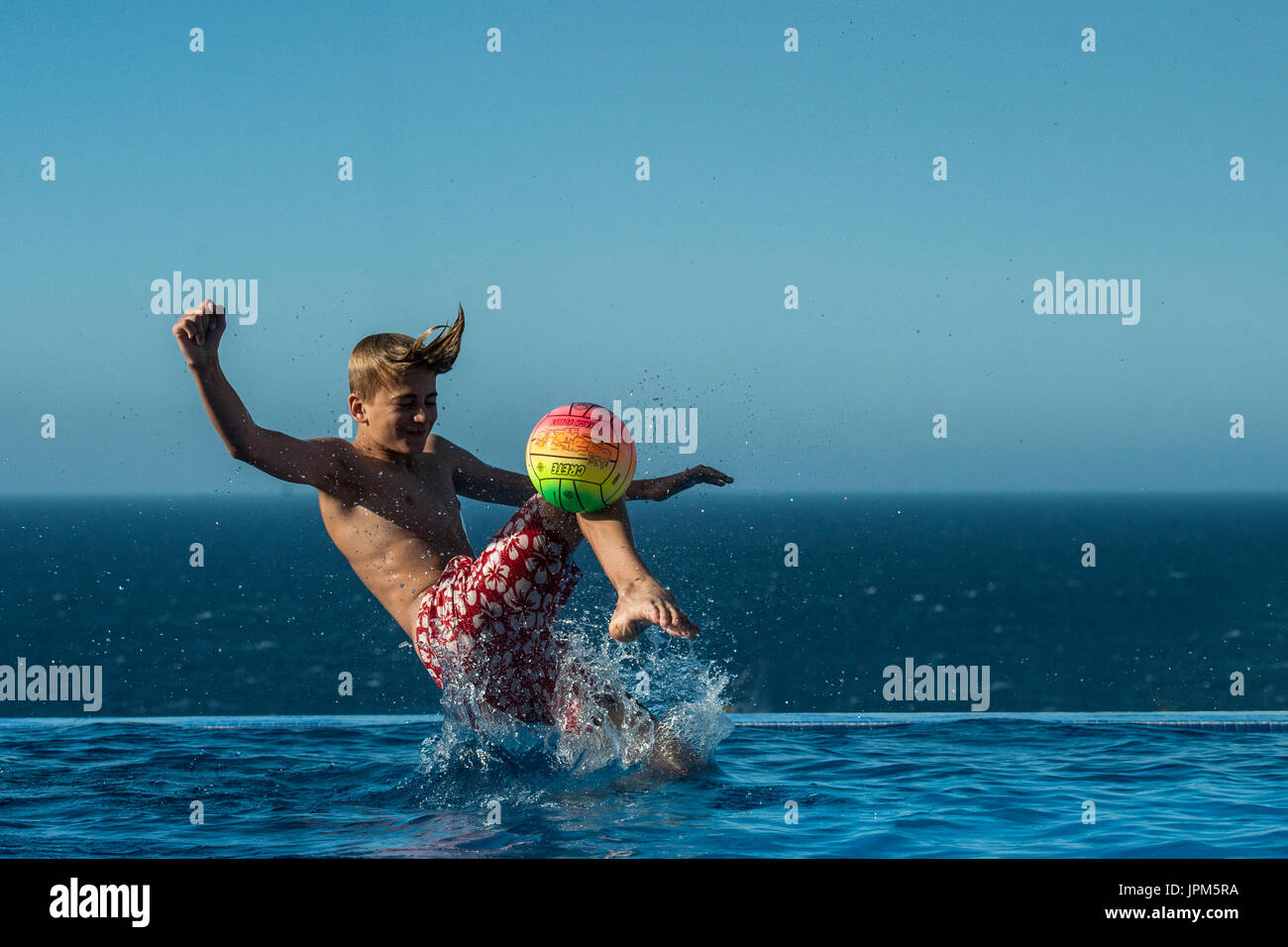 A boy jumps to kick a ball in an infinity pool in the summer, playing ...