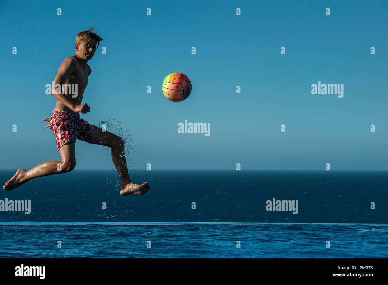 A boy jumps to kick a ball in an infinity pool in the summer, playing ...