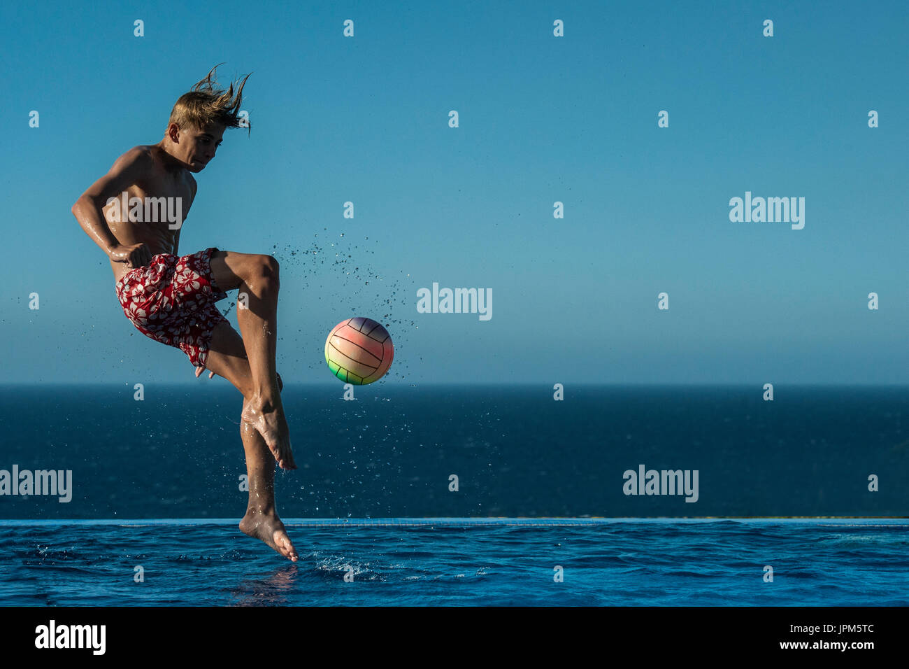 A boy jumps to kick a ball in an infinity pool in the summer, playing ...