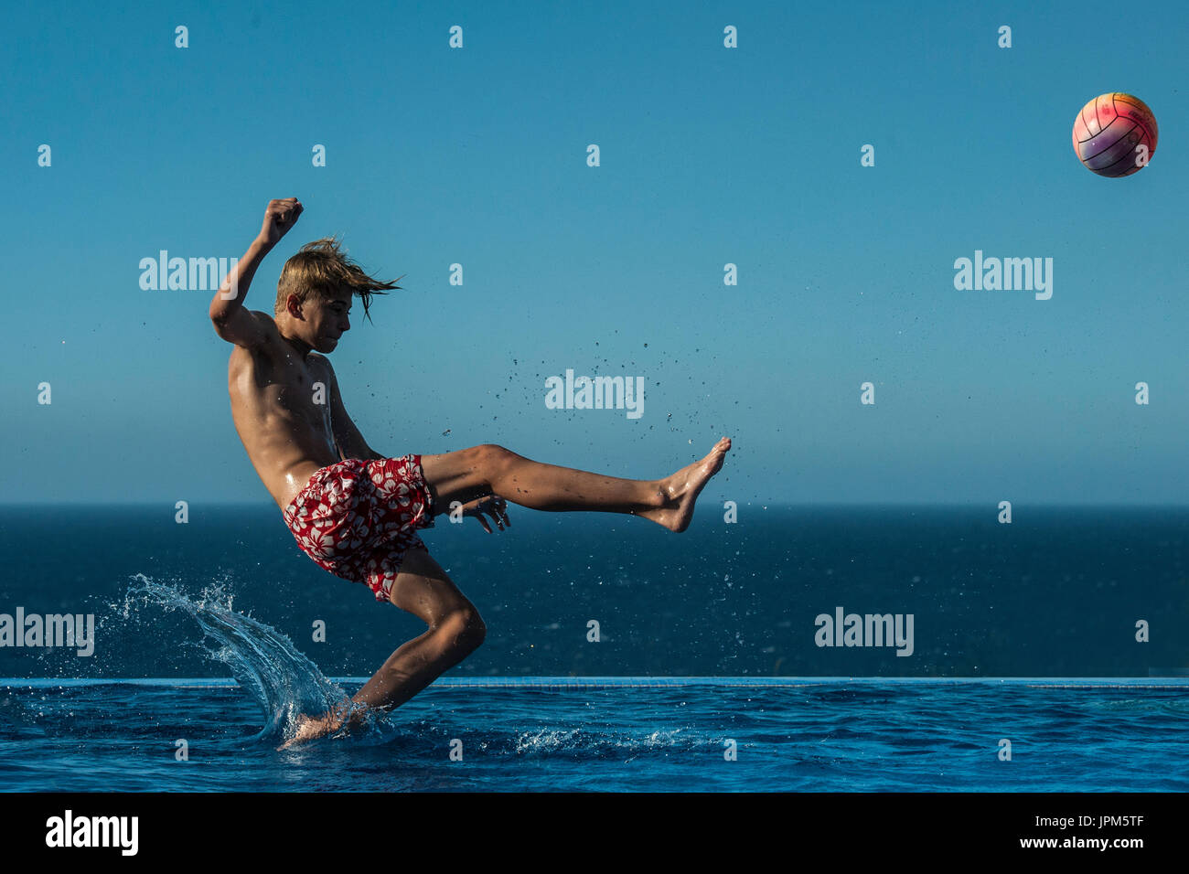 A boy jumps to kick a ball in an infinity pool in the summer, playing ...