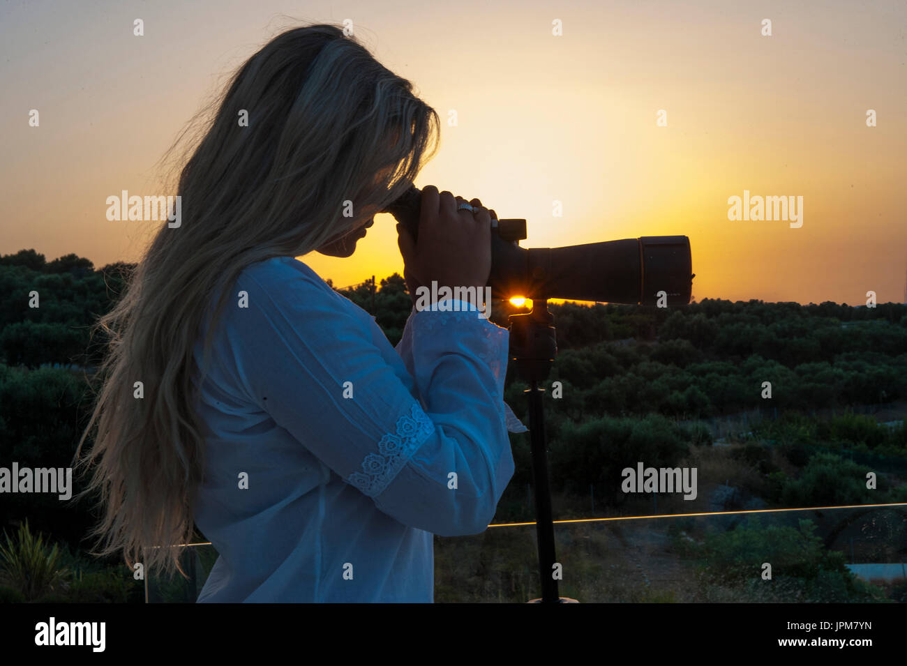 A pretty girl looks through a telescope at sunset Stock Photo - Alamy