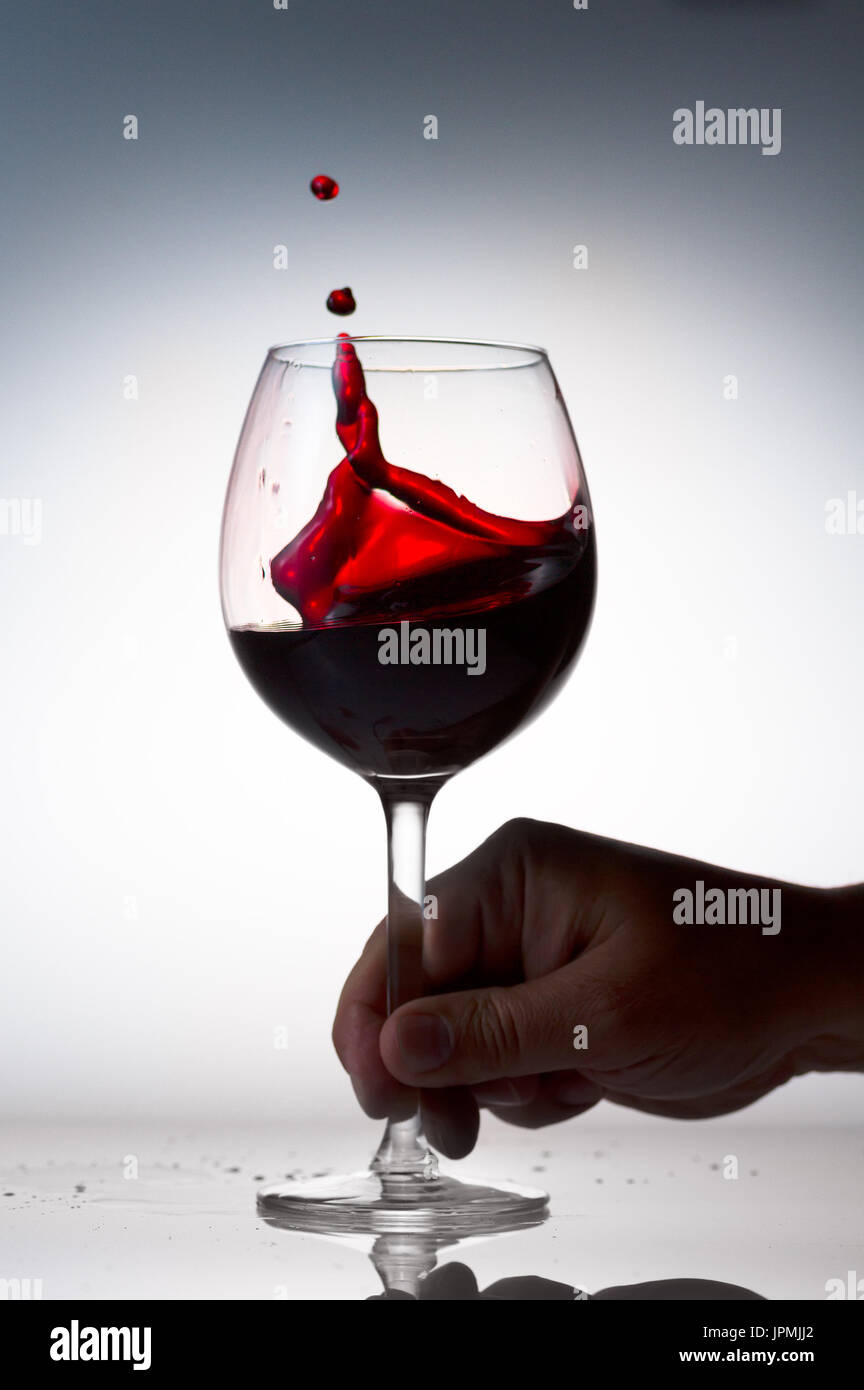 Someone Hand holding glass of red wine with splash Stock Photo - Alamy