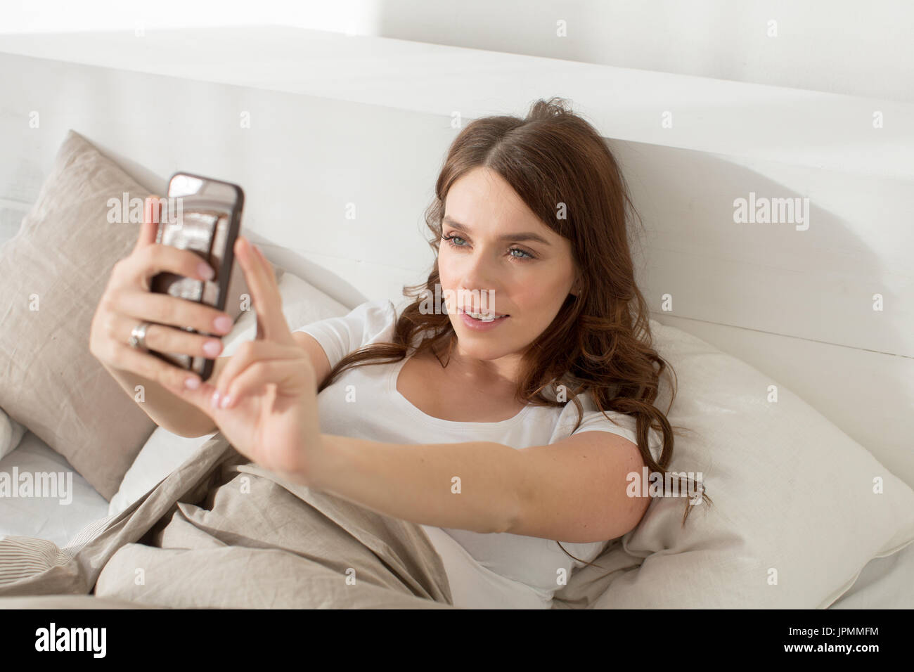 Female taking selfie lying in bed on a white background Stock Photo - Alamy