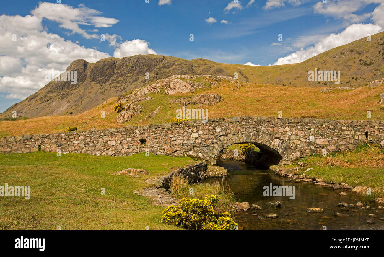 Arched stone bridge over trickling stream with rugged treeless hills of ...