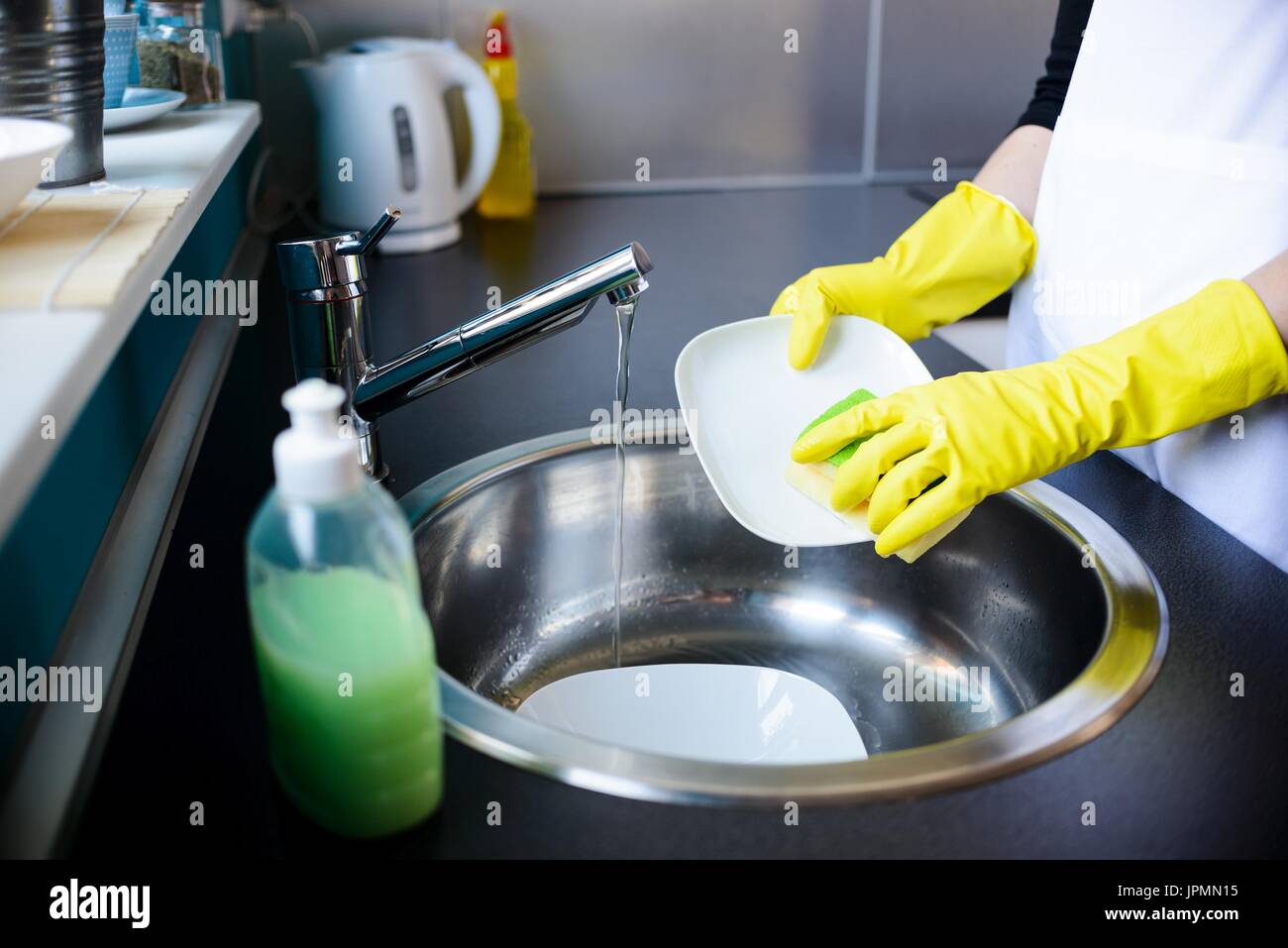 Woman in yellow protective rubber gloves washing dishes in the kitchen ...