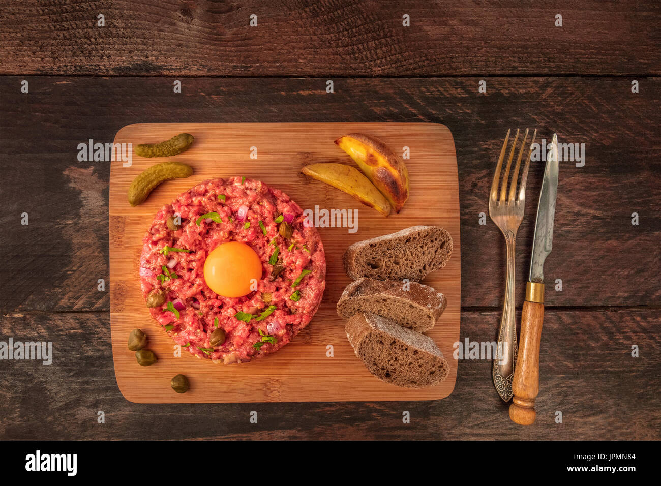 A photo of a steak tartare with a raw egg yolk, gherkins, capers, rye ...