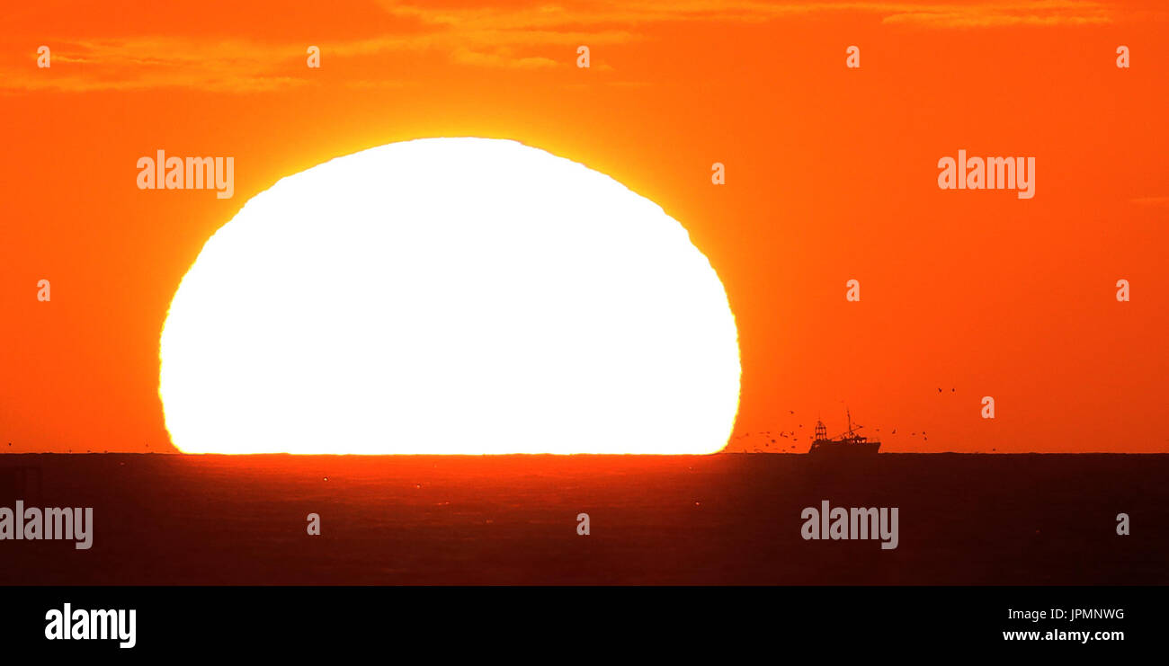 A fishing boat followed by seagulls on the Horizon heads back to port as the sun rises near ...