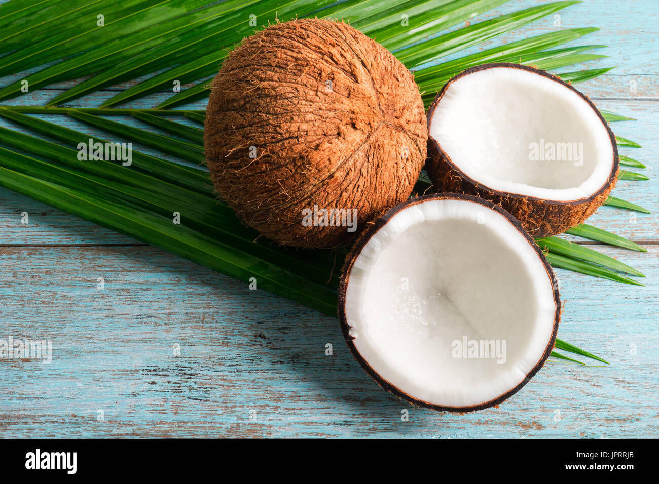 Coconut halves and green leaf on old wood background. Top view with ...