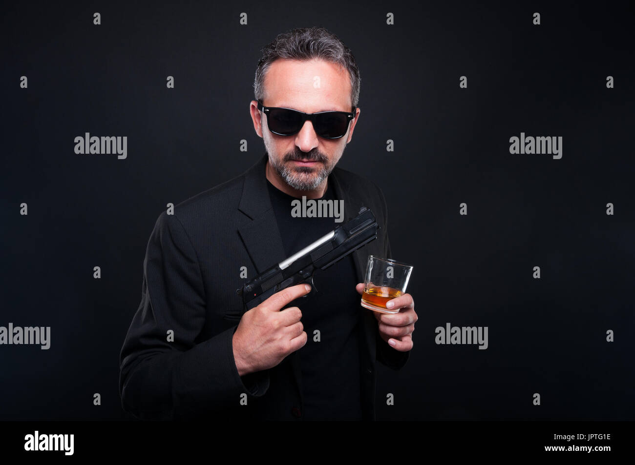 Confident gangster man with a glass of whisky and gun on black ...