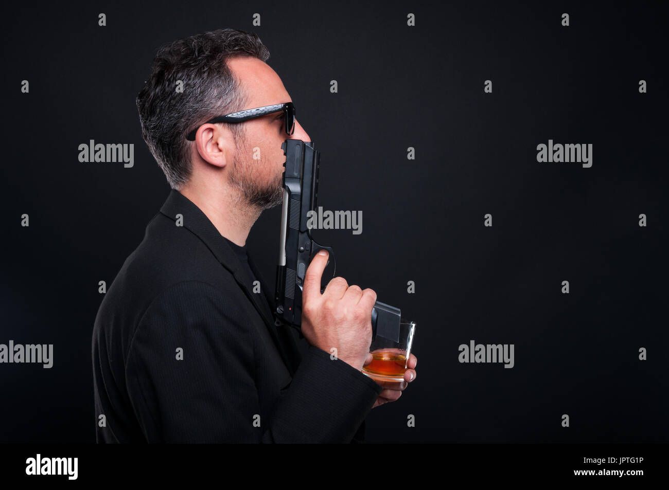 Side view of gangster dressed in black suit holding dangerous pistol or ...