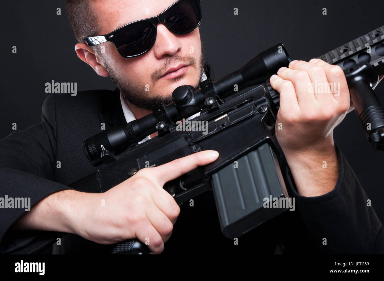 Expert hitman posing with rifle on his hands in close-up on dark ...