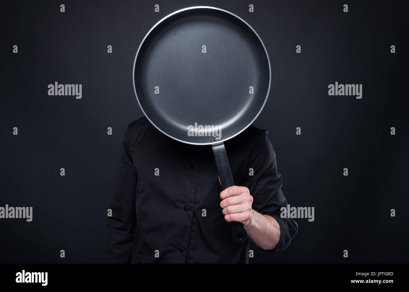 Male cook in uniform holding cooking pan in front of his face isolated ...