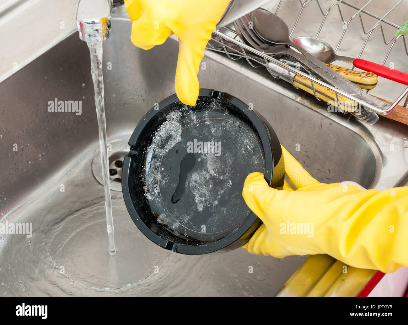 Housemaid holding dirty ashtray in the kitchen sink and cleaning it in ...
