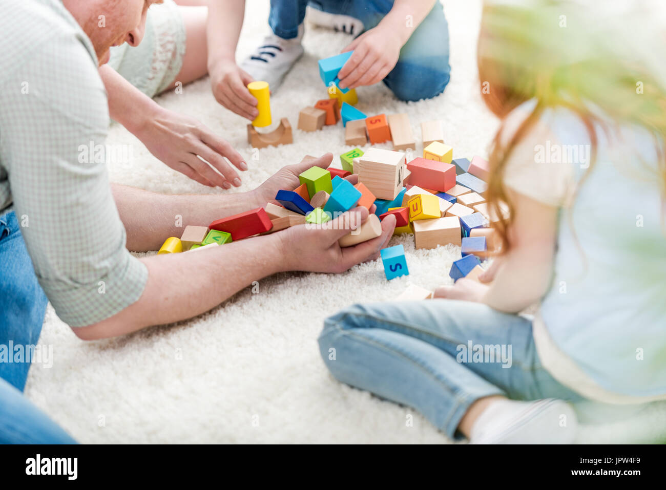 cropped view of family playing with constructor on floor at home ...