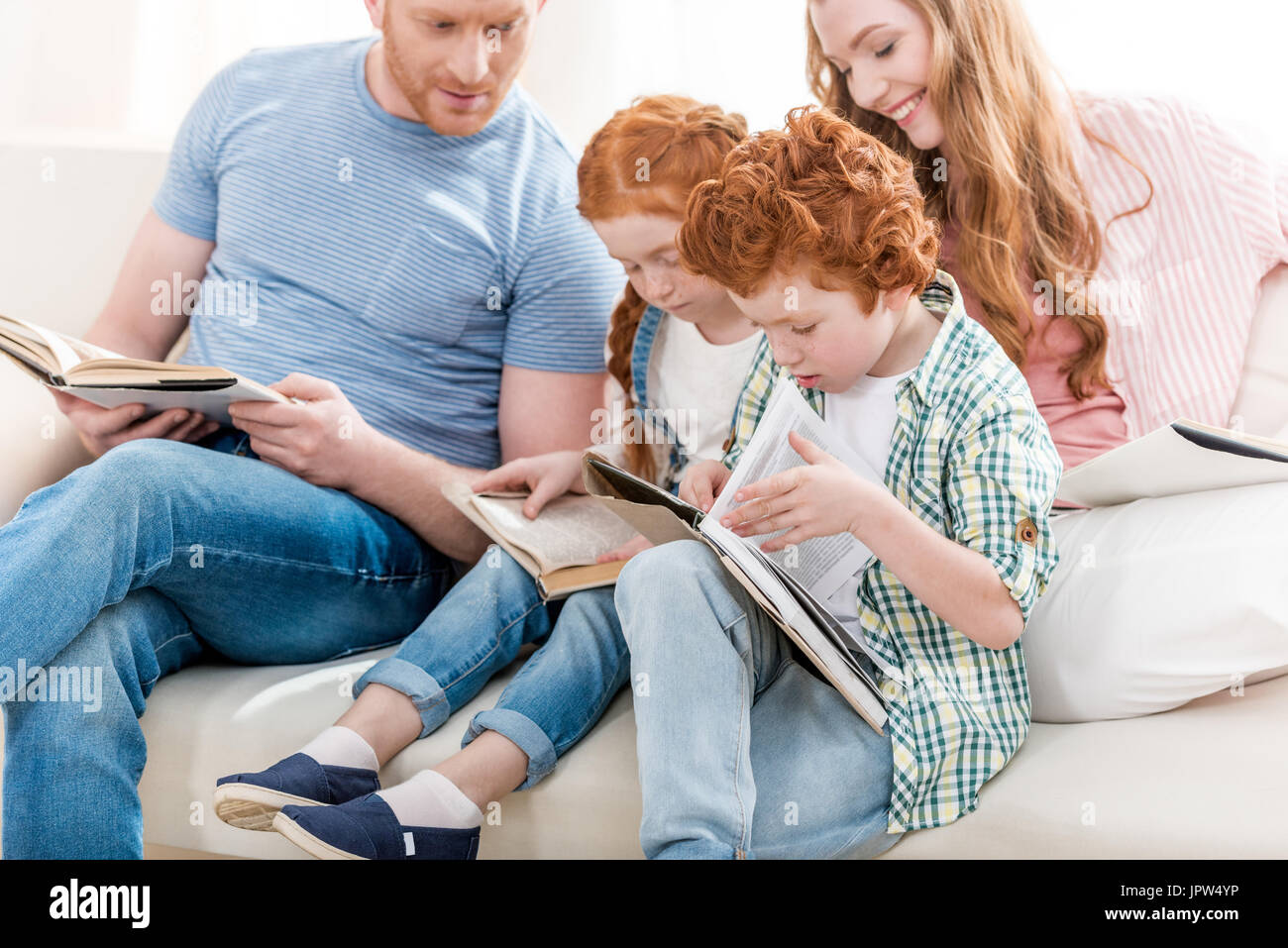 Beautiful redhead family sitting on sofa and reading books together ...