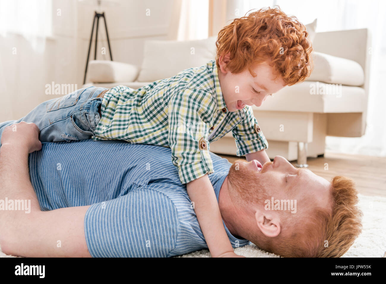 Happy redhead father and son having fun together on carpet at home ...
