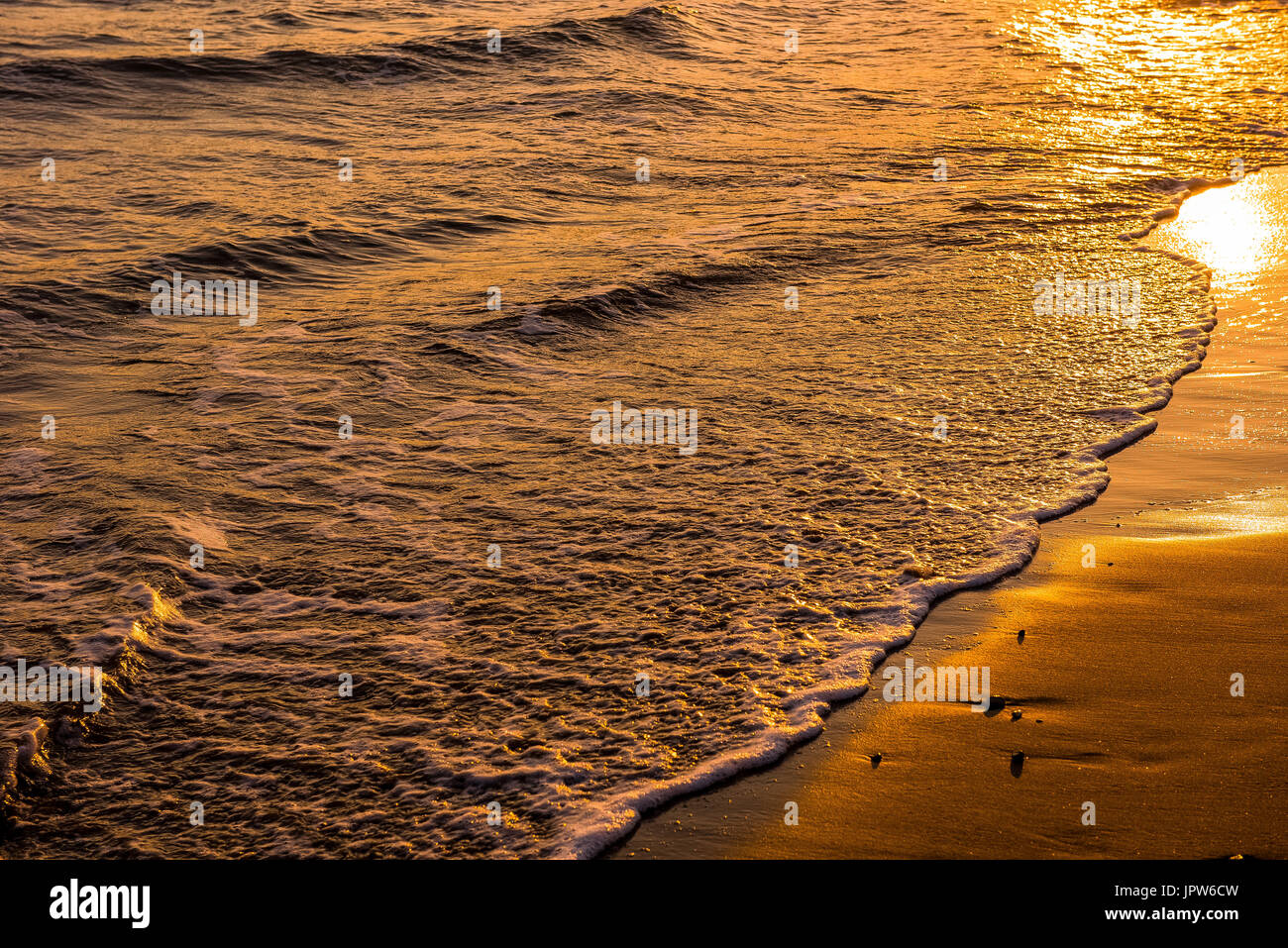 Waves approaching beach sand during golden sunset. Saturated image ...