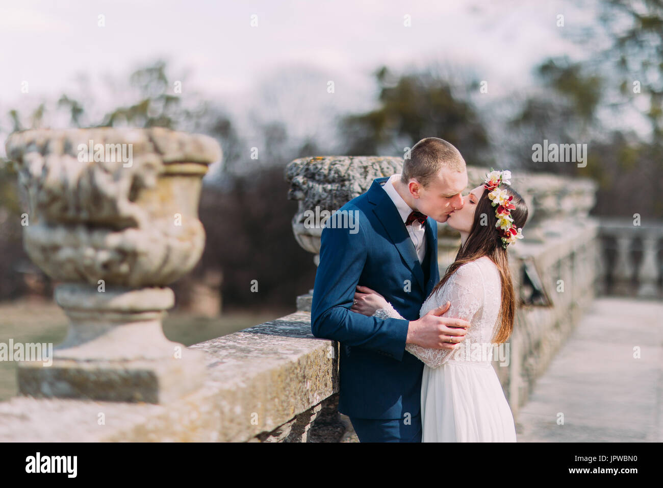 Wedding portrait of stylish newlywed couple passionately kissing at old ...