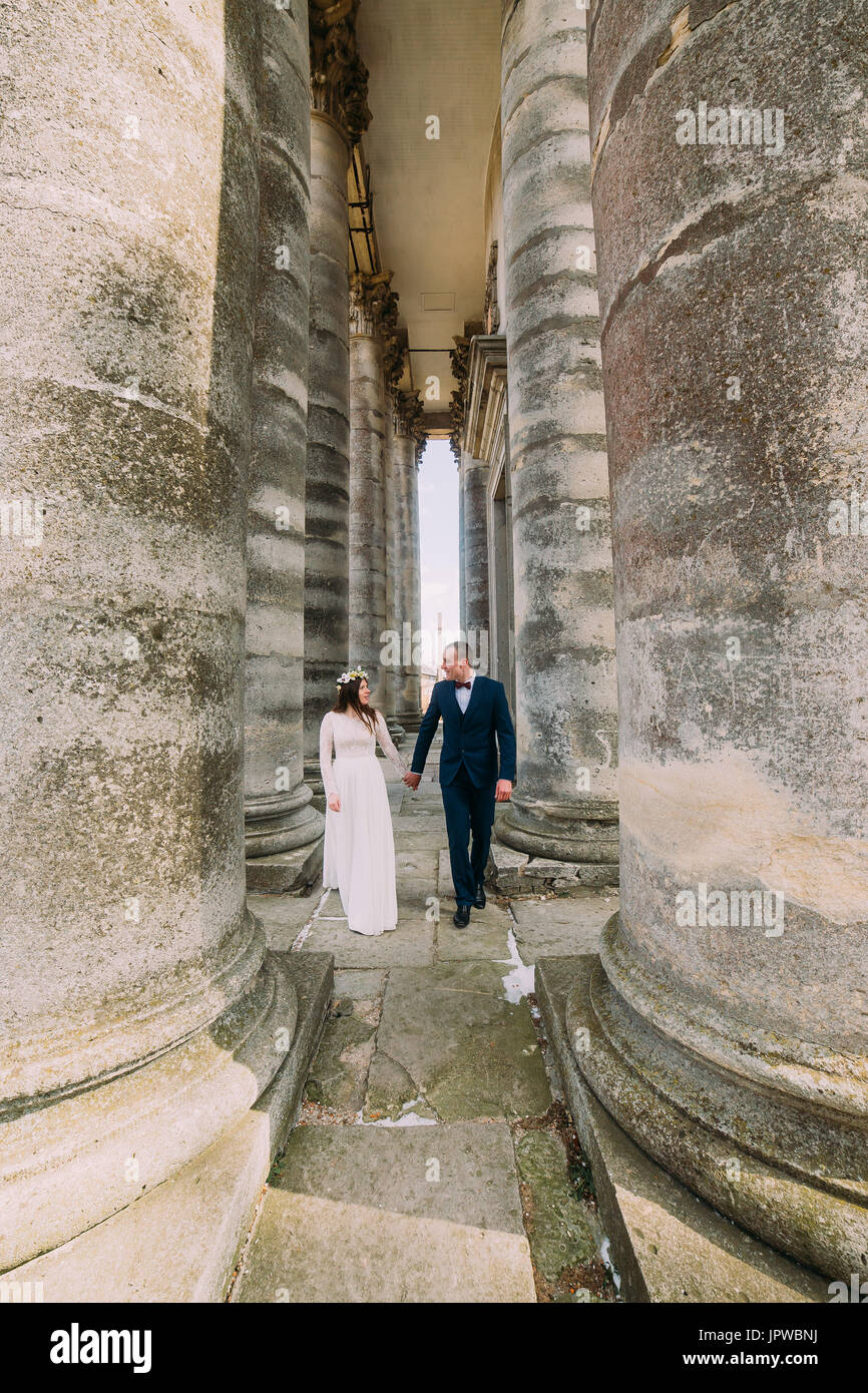 Young wedding couple posing between rows of antique building columns ...