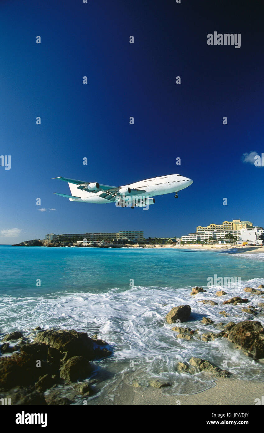 a Boeing 747 on very low final-approach over a beach, sea and rocks ...