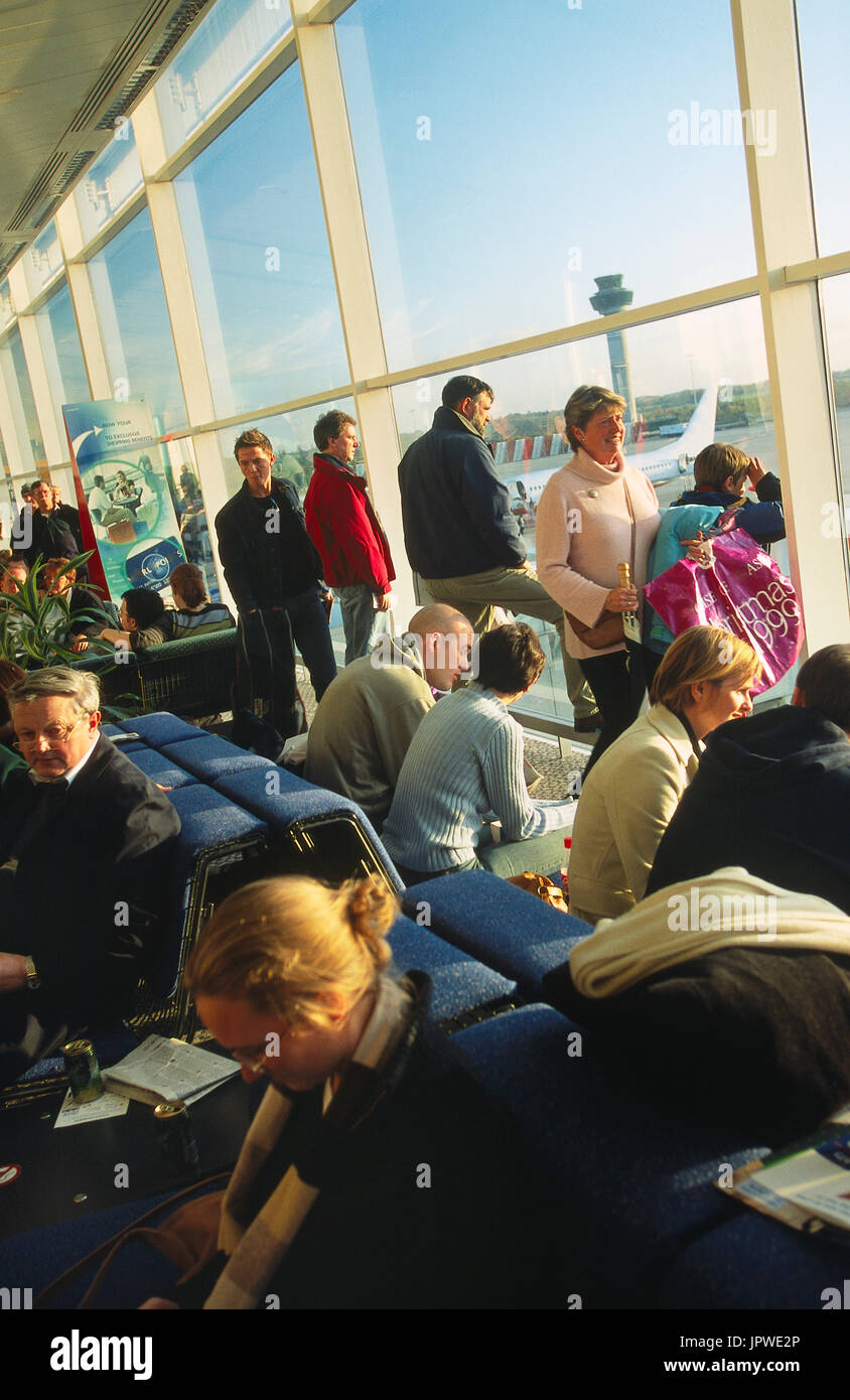 passengers waiting in a crowded gate departure-lounge next to windows ...