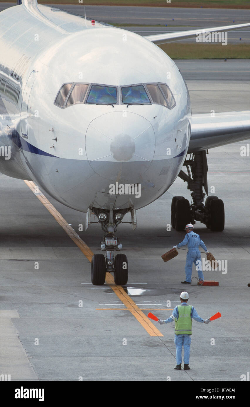 marshaller waving batons at an ANA Boeing 767 taxiing and a man with ...