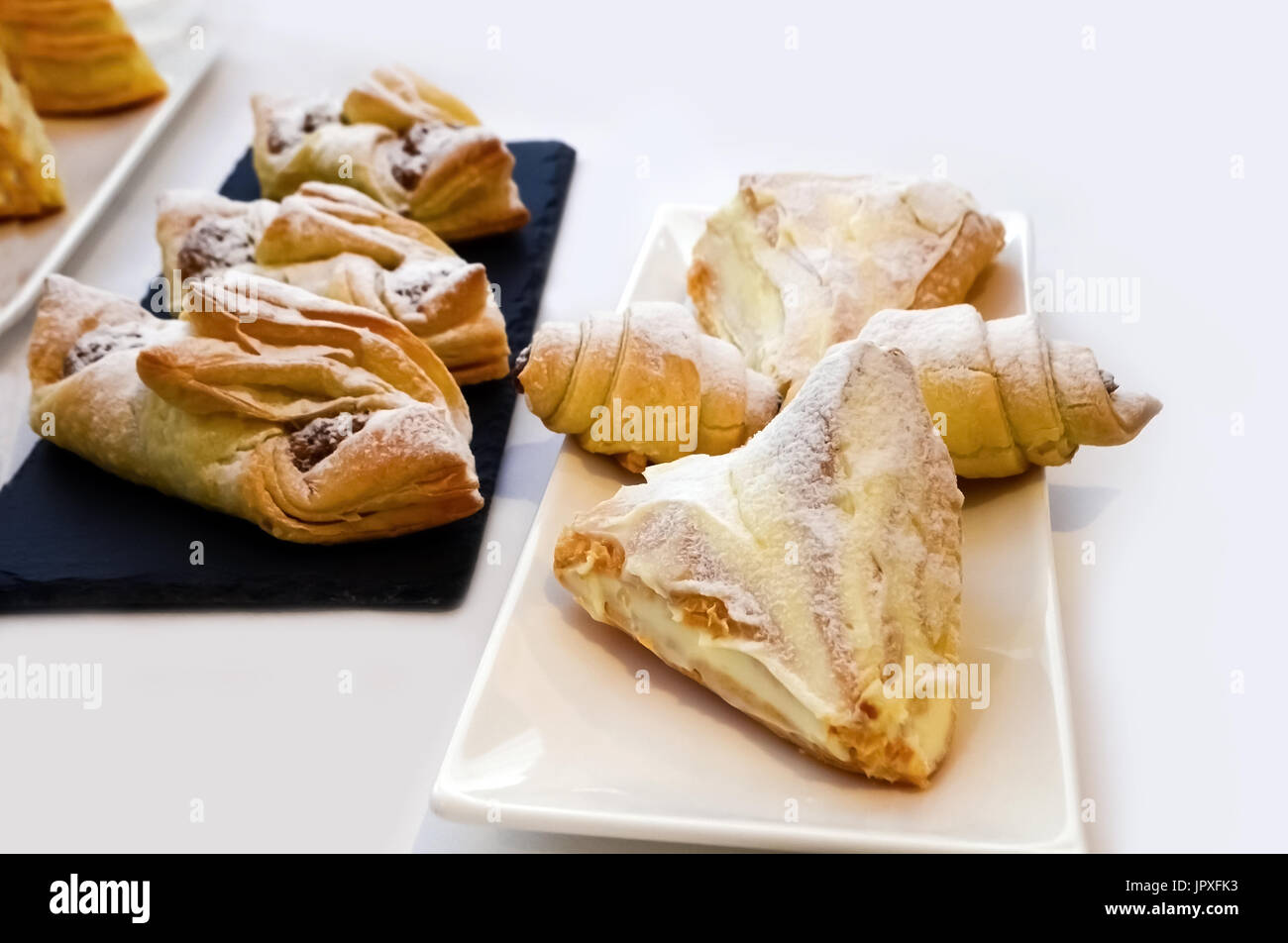 Baked pastry, buns sprinkled with powdered sugar on long plates of ...