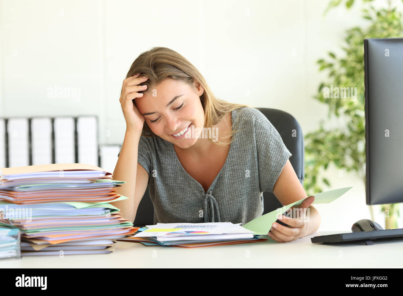 Front view portrait of a happy employee reading report sitting in a ...