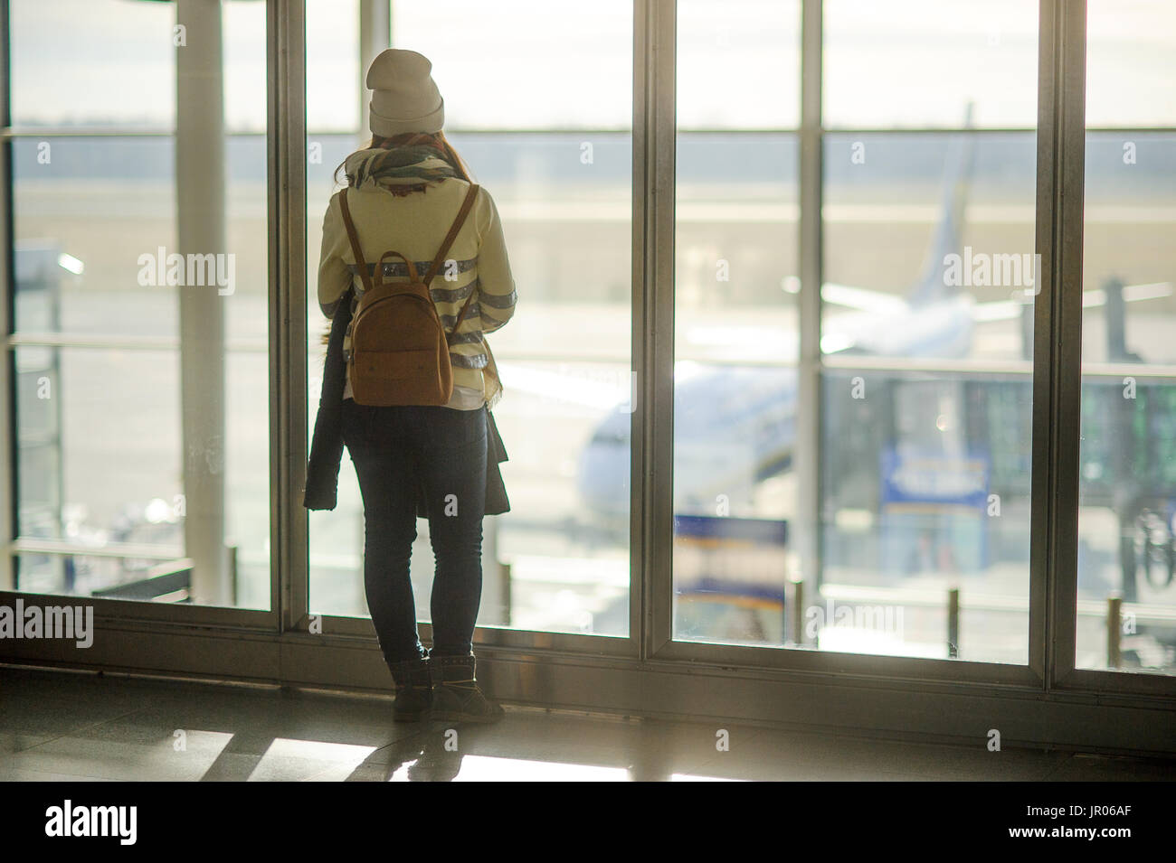 A woman with a backpack behind her is standing by the big window at the ...