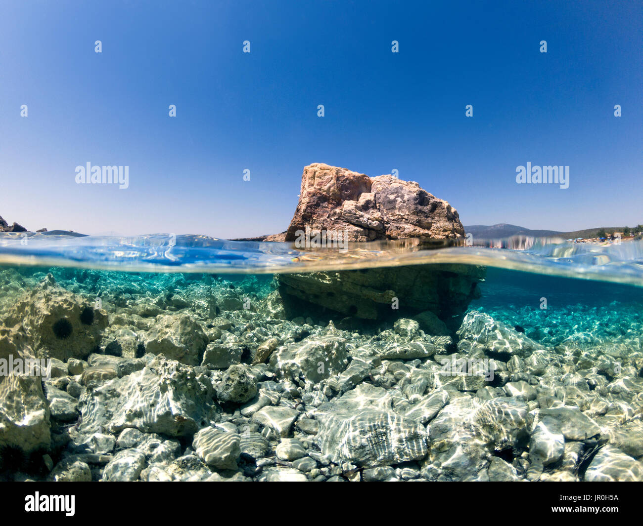 Half underwater in the sea a big rock and small rocks and sea urchins ...