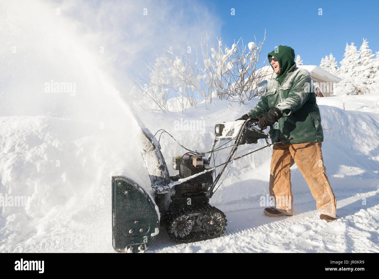 A Man Happily Using His Snowblower In Front Of His House; Alaska ...