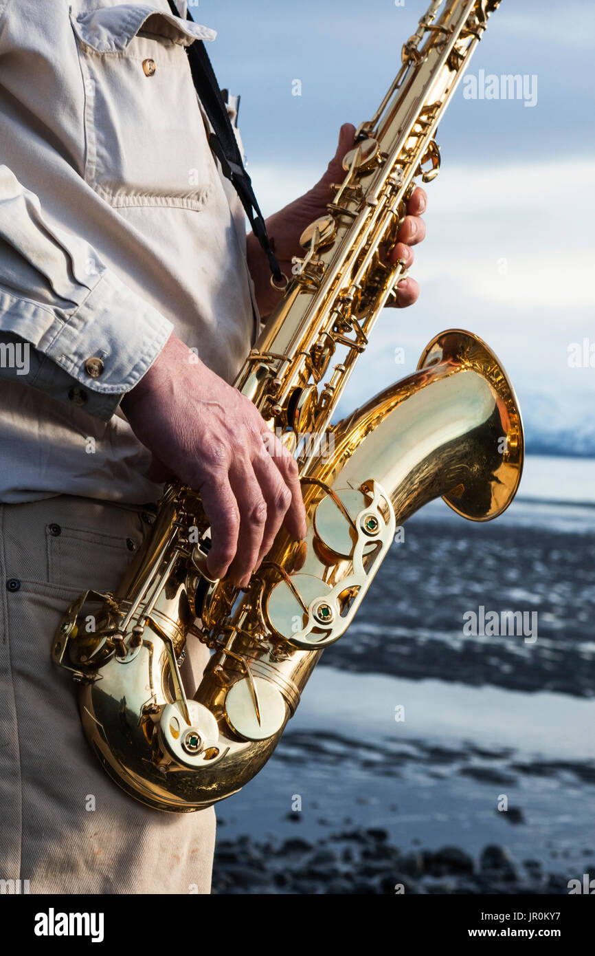 A Man Stands With A Saxophone On The Beach At The Water's Edge; Alaska ...
