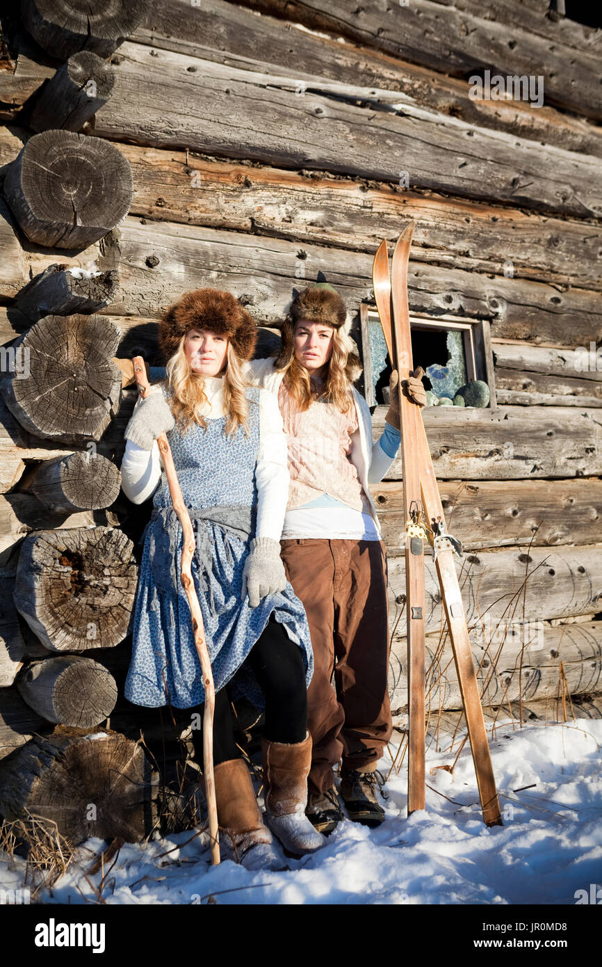 Portrait Of Two Girls Standing By A Log Cabin Wearing Fur Hats Holding ...