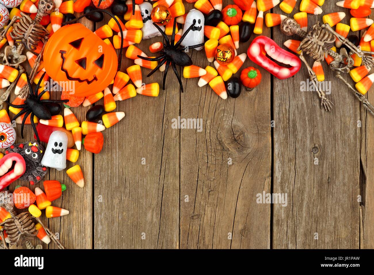 Halloween candy and decor top corner border against a rustic wood ...