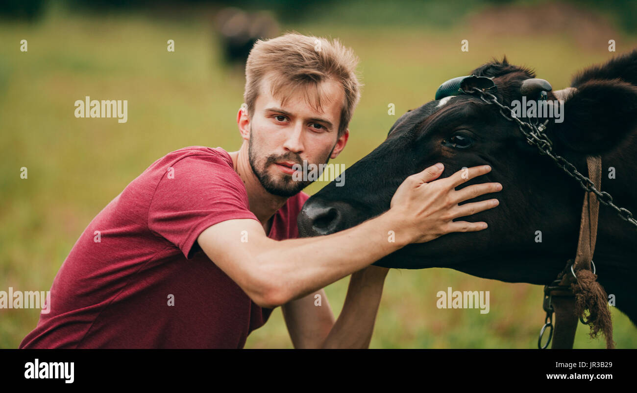 Portrait of young man caressing black cow on head Stock Photo - Alamy