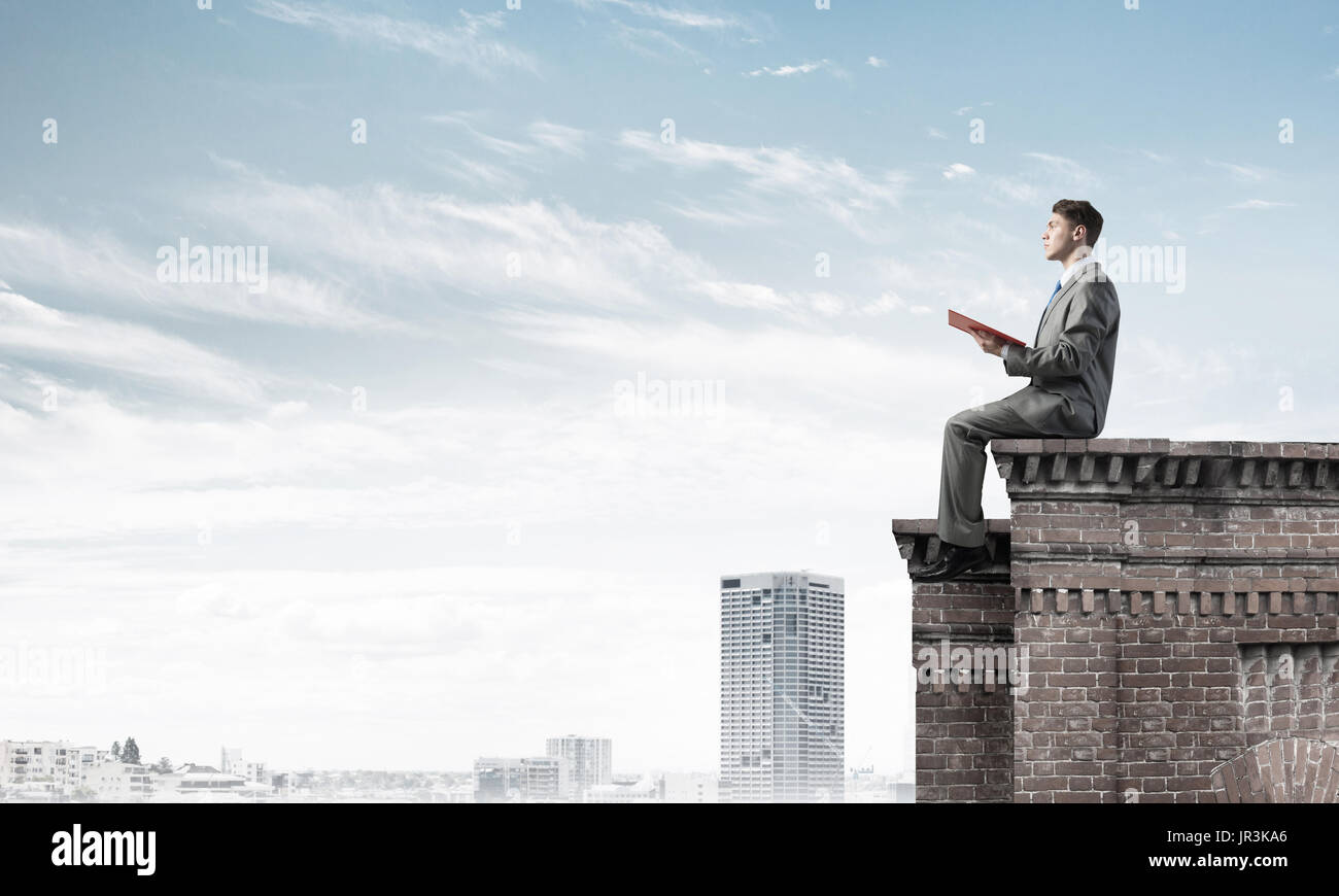 Man on roof edge reading book and cityscape at background Stock Photo ...
