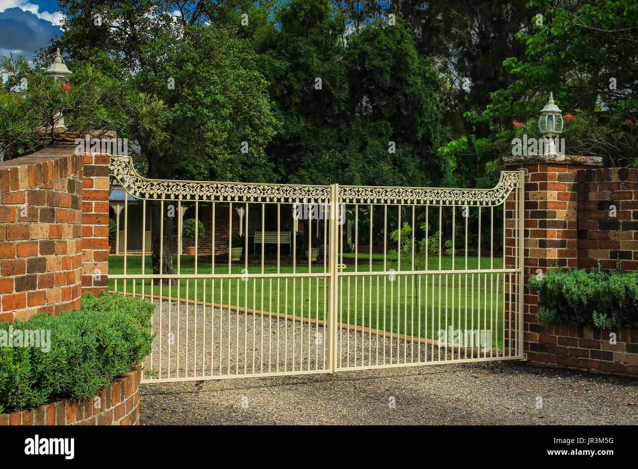 Metal driveway entrance gates set in brick fence with garden trees in ...