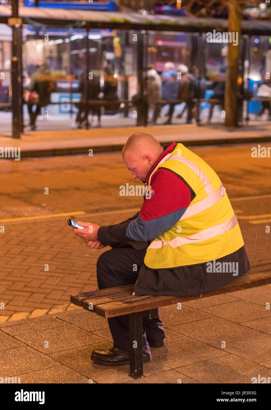 Bus driver wearing a uniform sitting on a bench reading his mobile ...