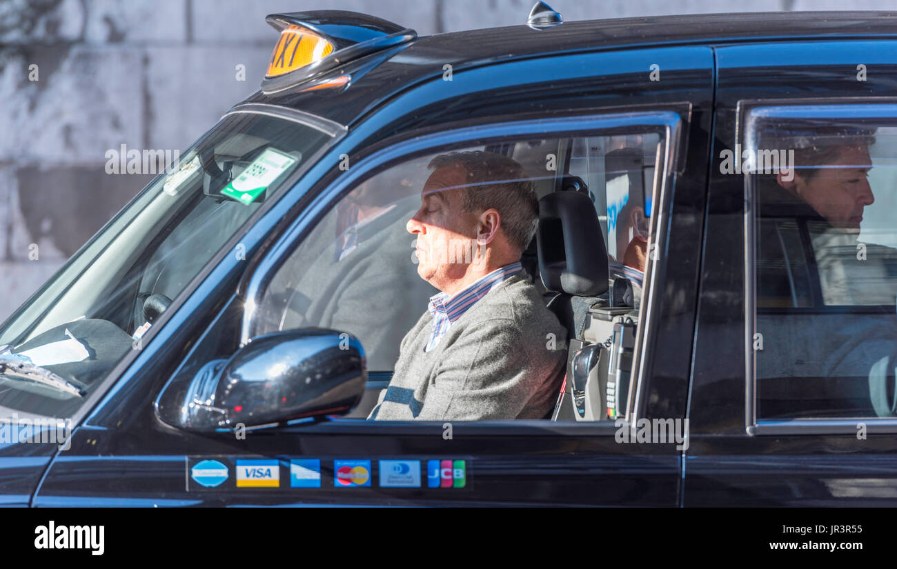 A black cab driver resting at the wheel in busy traffic in London with ...