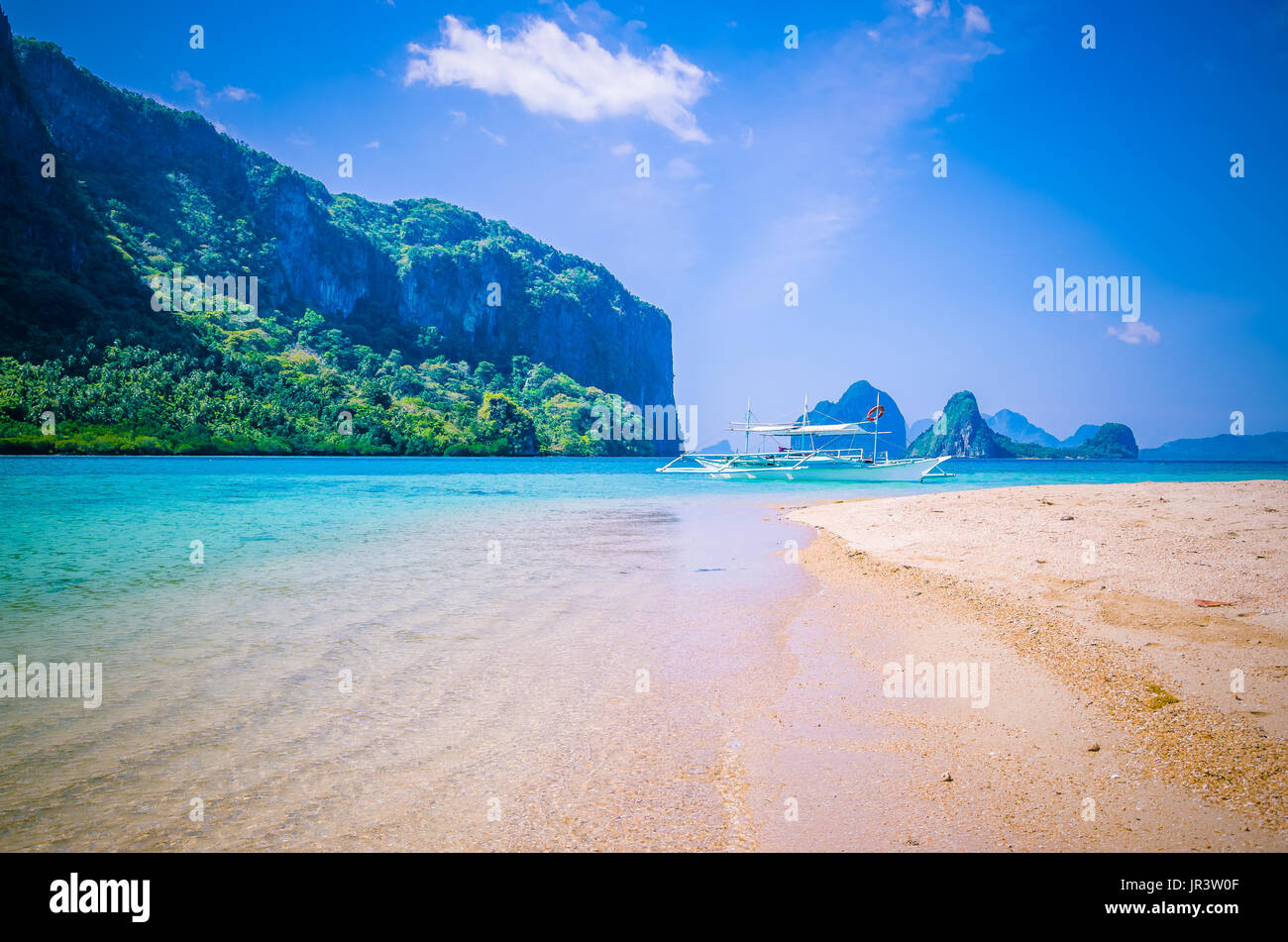 Traditional banca boat in clear water at sandy Beach near El Nido ...