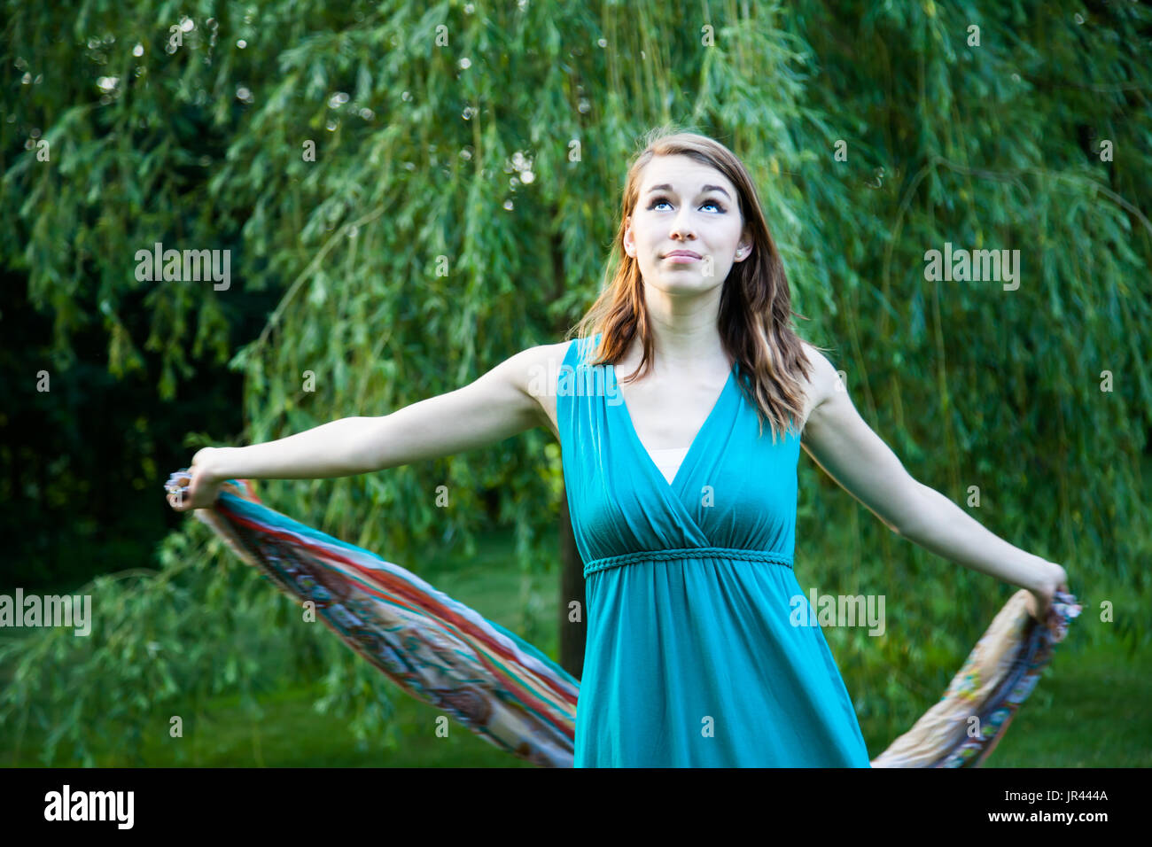 Beautiful girl is slowly spinning around in front of a willow tree ...