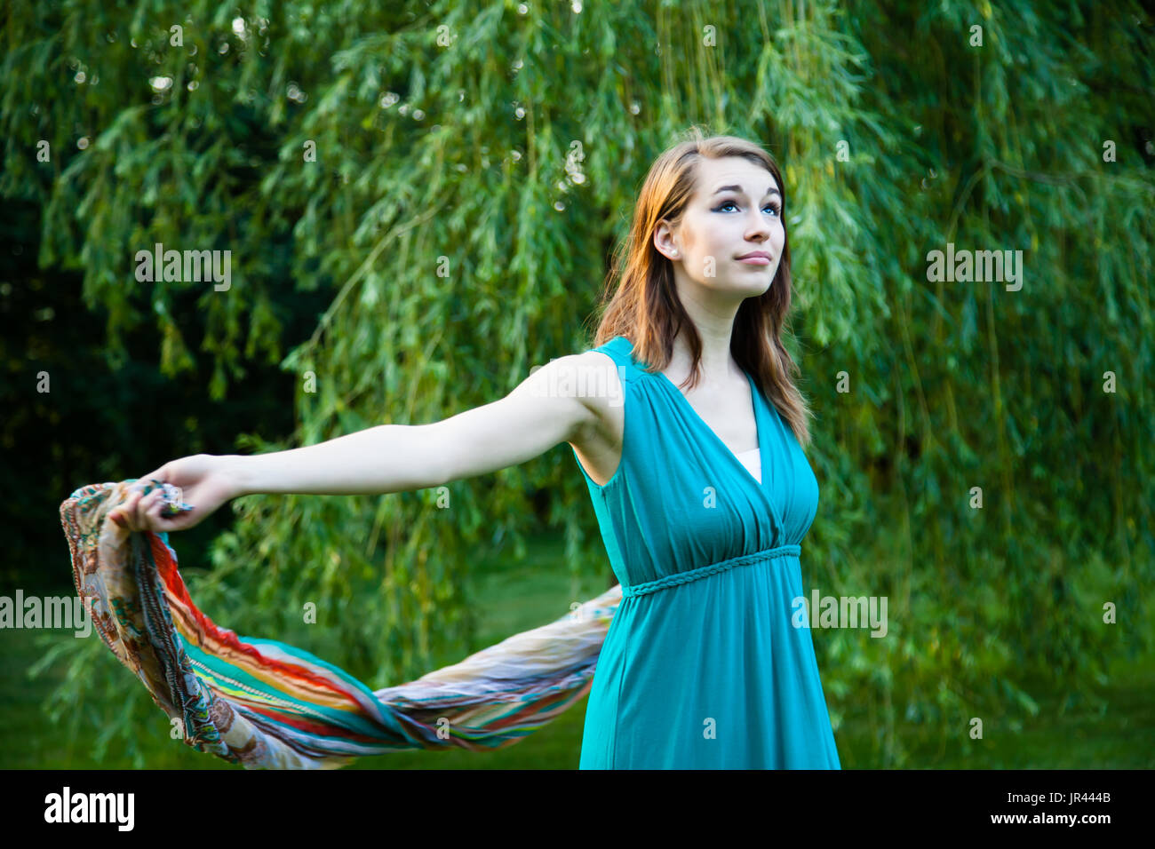 Beautiful girl is slowly spinning around in front of a willow tree ...