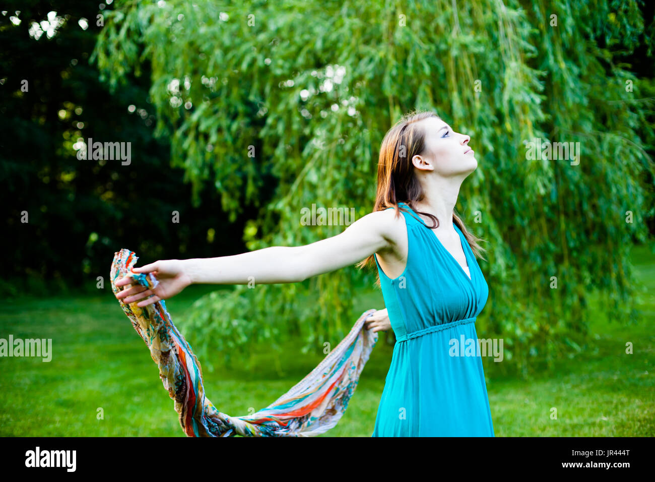 Beautiful girl is slowly spinning around in front of a willow tree ...